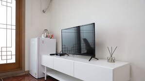 Uma sala de estar moderna com televisão de tela plana em um armário branco, um refrigerador pequeno e uma janela com padrão geométrico.