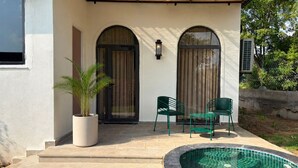 Uma casa com alpendre, duas portas em arco, uma piscina pequena e duas cadeiras.