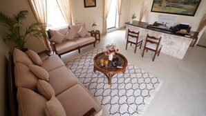 Uma sala de estar com sofá, uma mesa de centro com flores, área de jantar com cadeiras e cozinha com balcão.