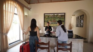 Uma receção com uma recepcionista, uma janela com cortinas e um quadro na parede.