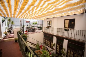 Um pátio com toldo listrado, móveis de exterior, plantas em vasos e uma escadaria que leva a um andar superior.