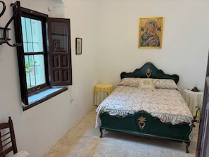 A bedroom with a bed, a window with a view, a wall-mounted picture, and a bedside table.