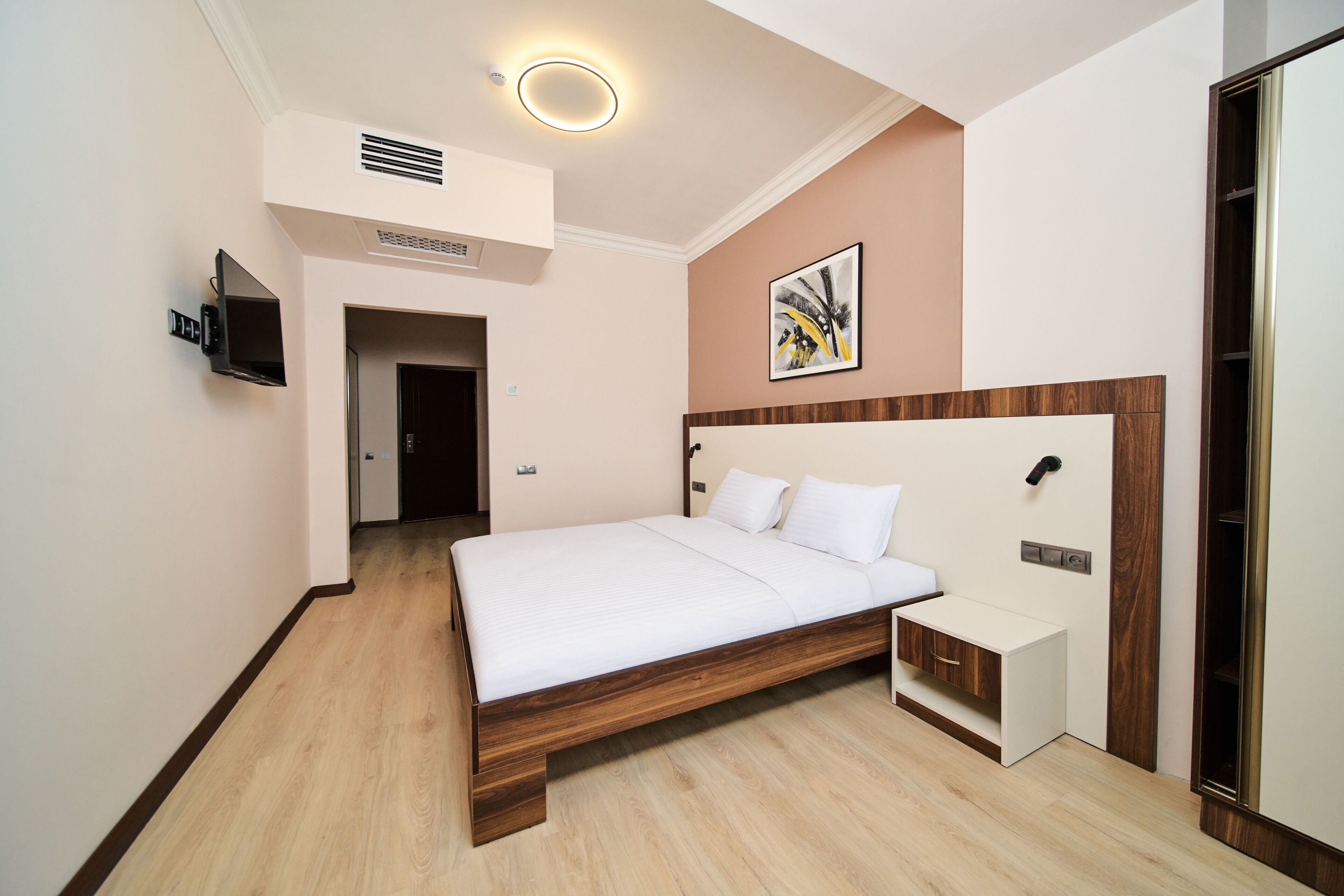 Quarto de hotel moderno com uma cama grande, uma mesinha de cabeceira, uma televisão de tela plana na parede e um lustre no teto.