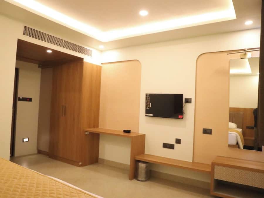 Quarto de hotel com uma cama, televisão na parede, guarda-roupa de madeira e um espelho.
