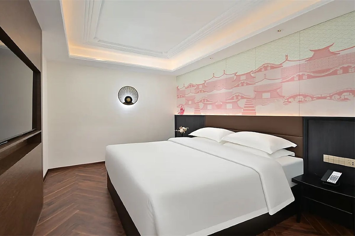 Quarto de hotel com uma cama grande, luminária fixada na parede e um objeto decorativo na parede.