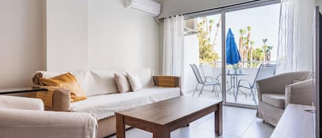 Uma sala de estar moderna com um sofá, uma mesa de centro de madeira e uma varanda com cadeiras e um guarda-sol azul.
