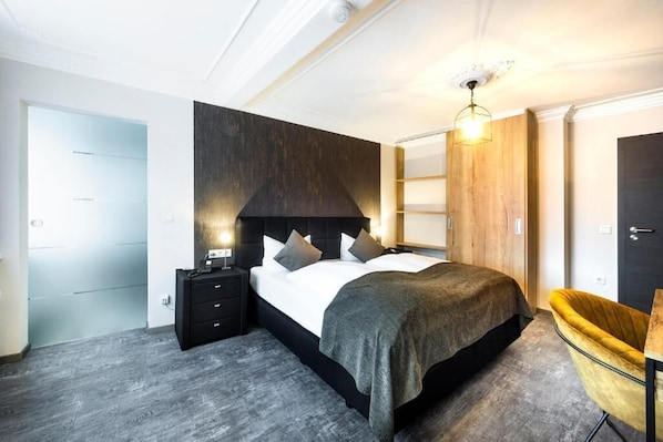 Um quarto moderno com uma cama grande, mesas de cabeceira, um guarda-roupa de madeira e uma cadeira amarela única.