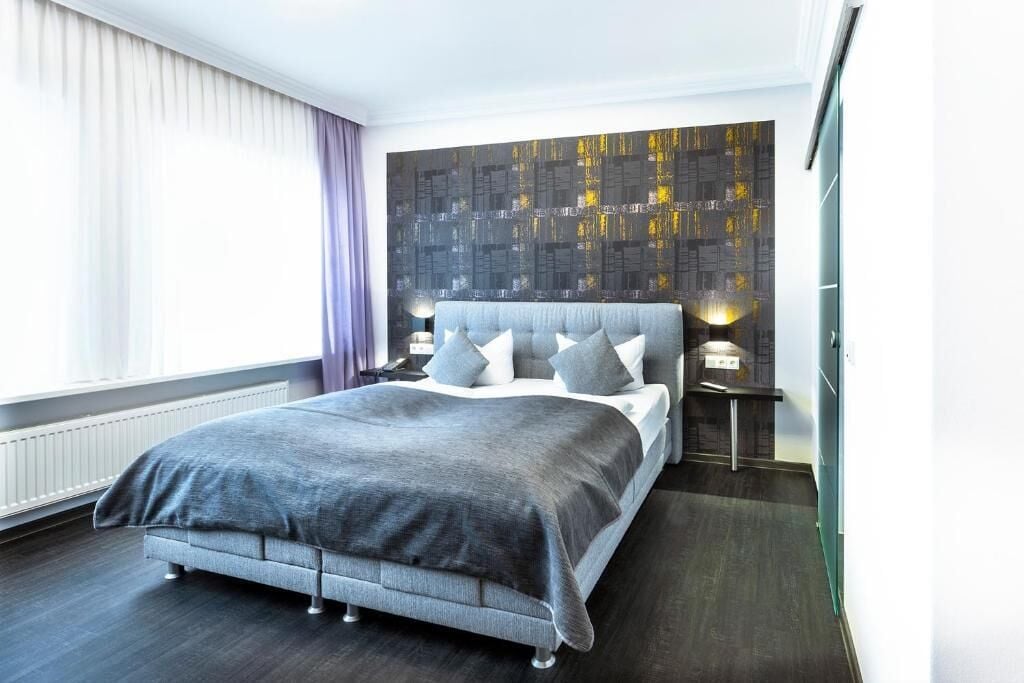 Quarto moderno com uma cama grande, cabeceira estampada e vista para o exterior.