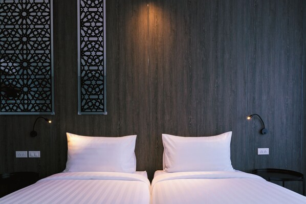 Quarto de hotel com parede de madeira, duas camas com lençóis brancos, um painel decorativo na parede e duas luminárias fixadas na parede.