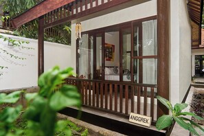 Uma estrutura de madeira com varanda, uma cama e uma placa com a inscrição 'ANGGREK'.