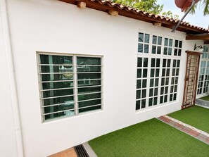 Edifício branco com grandes janelas e uma pequena área de jardim com grama sintética.
