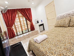 Quarto de hotel com uma cama, televisão, escrivaninha e janela com cortinas vermelhas.