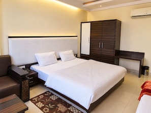 Quarto de hotel com cama grande, mesa de cabeceira, guarda-roupa e escrivaninha.
