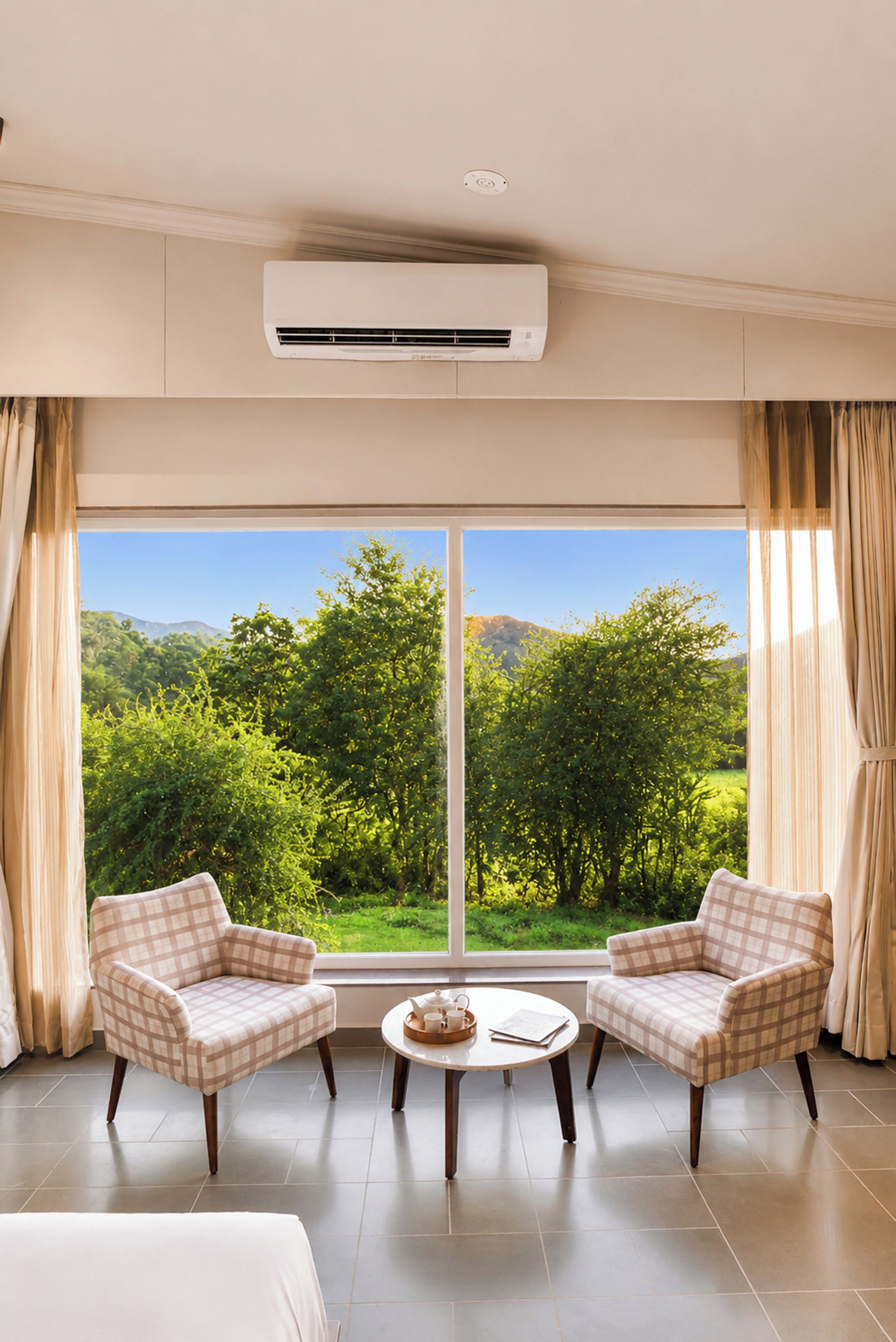 Quarto com duas poltronas xadrez voltadas para uma janela grande com vista para uma paisagem verde.