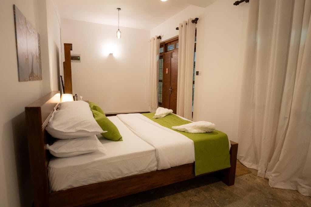 Quarto com cama de madeira, roupa de cama branca, um travesseiro verde e uma toalha branca.