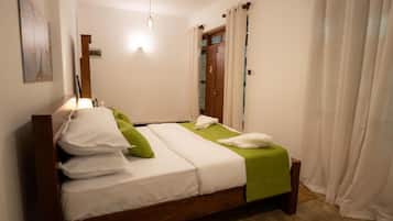 Quarto com cama de madeira, roupa de cama branca, um travesseiro verde e uma toalha branca.