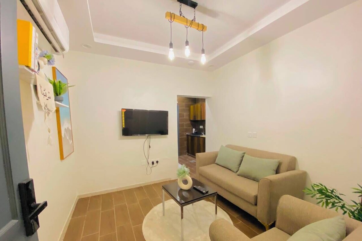 Uma sala de estar com sofá, mesa de centro, televisão de tela plana e luminária no teto.