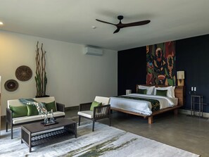 Quarto moderno com cama grande, sofá, mesa de centro e ventoinha no teto.