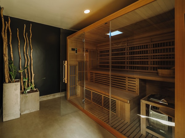 Uma sauna com bancos de madeira, porta de vidro e um vaso de concreto com plantas.