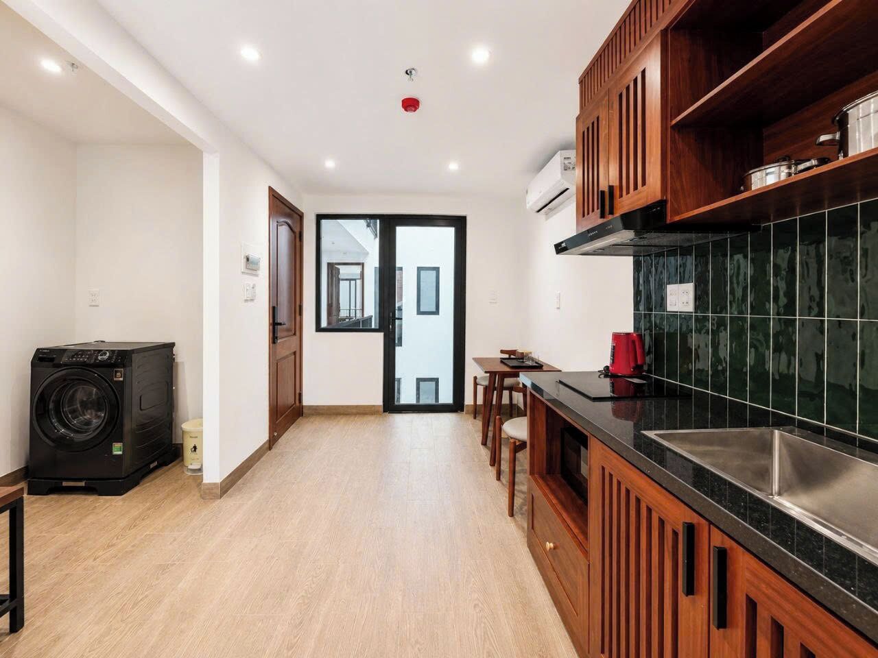 Cozinha com máquina de lavar, área de refeições com cadeiras e vista através de uma porta.