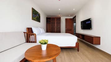 Quarto de hotel com cama, sofá, mesa de madeira com planta, televisão e guarda-roupa.