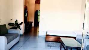Sala de estar com sofá, mesa de centro e uma planta. Escada leva a outro cômodo.