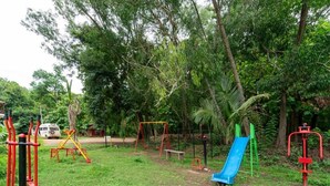Um parquinho ao ar livre com diversos equipamentos, incluindo baloiços, escorregador e estruturas para escalar.