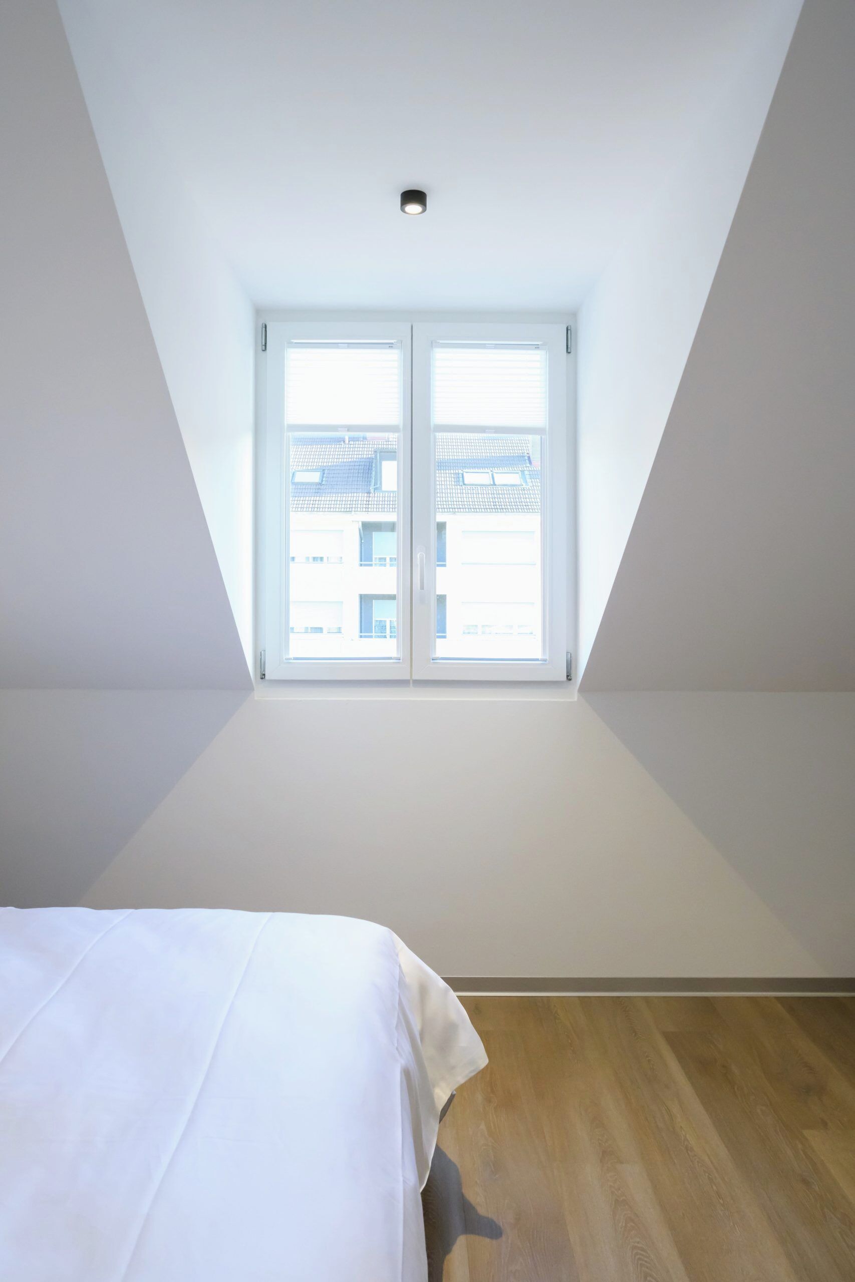 Um quarto com teto inclinado, claraboia, cama e piso de madeira.