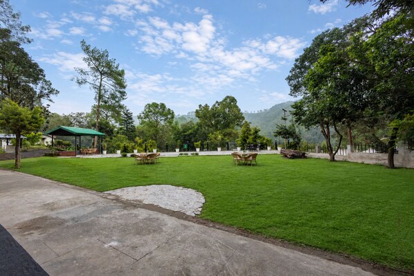 Uma área gramada bem cuidada, com mesas de piquenique e um gazebo.
