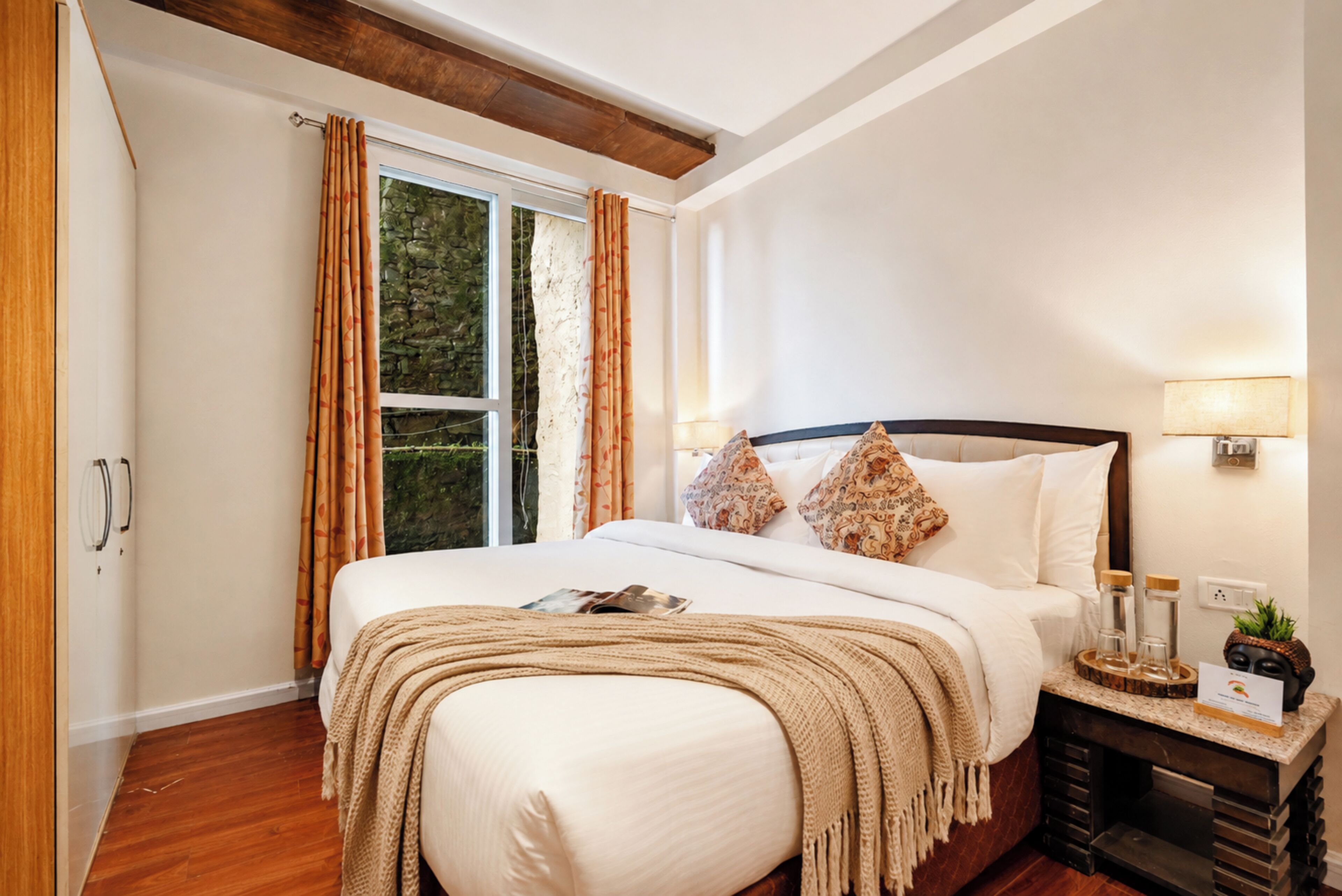 Um quarto com uma cama grande, uma mesa de cabeceira com abajur e uma janela com cortinas.