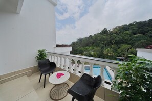 Uma varanda com duas cadeiras, uma mesa pequena e vista para uma piscina e área arborizada.