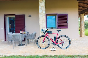 Um pátio ao ar livre com mesa e cadeiras, uma bicicleta vermelha e um muro de pedra.
