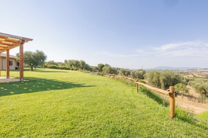 Uma área externa gramada com uma pérgola de madeira e vista para o campo.