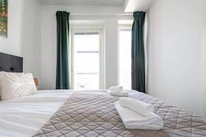 Quarto de hotel com cama, duas almofadas, uma toalha dobrada e vista para o exterior.