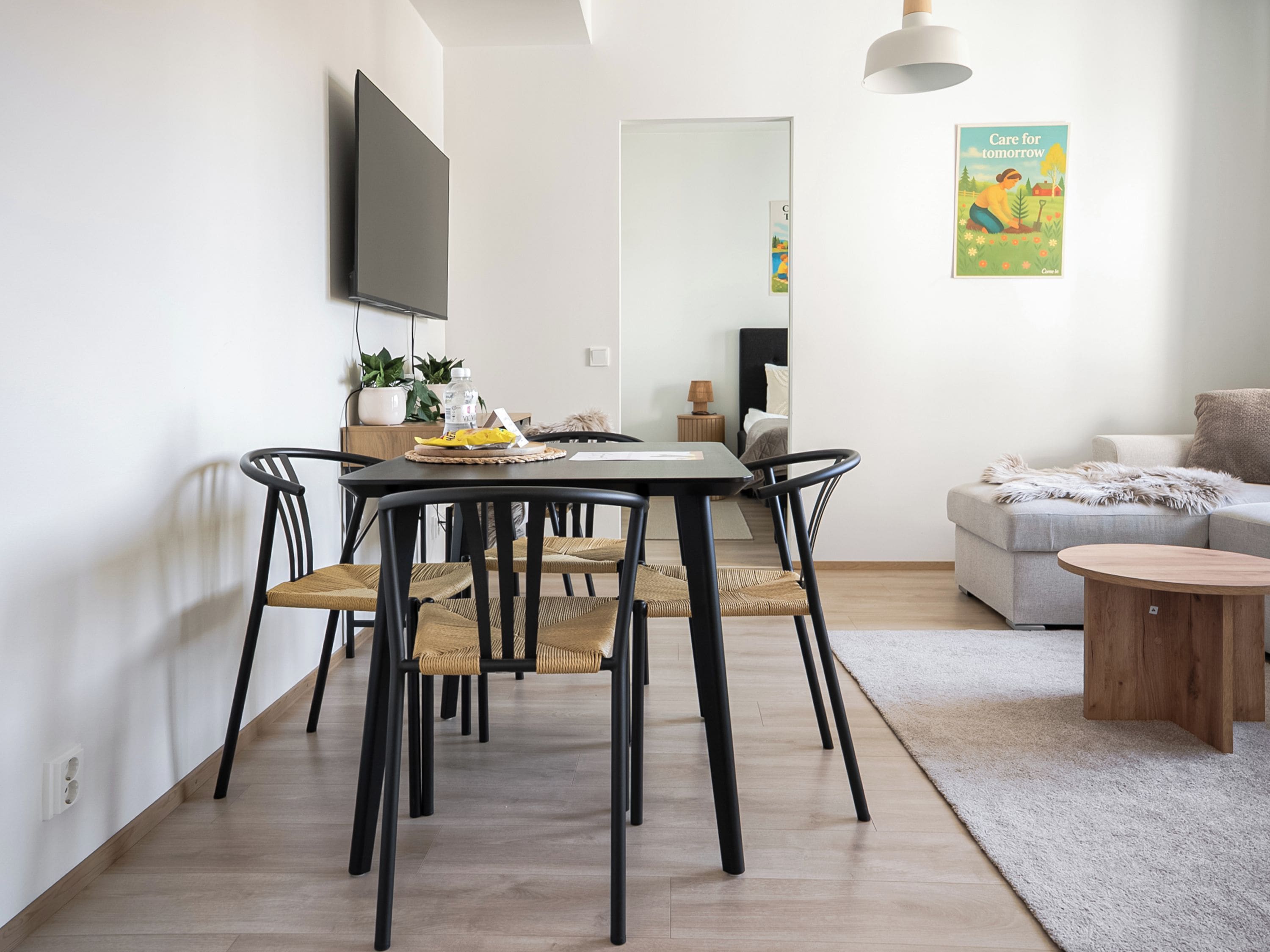 Uma sala de estar moderna com área de jantar, televisão de tela plana na parede, sofá e um pôster.