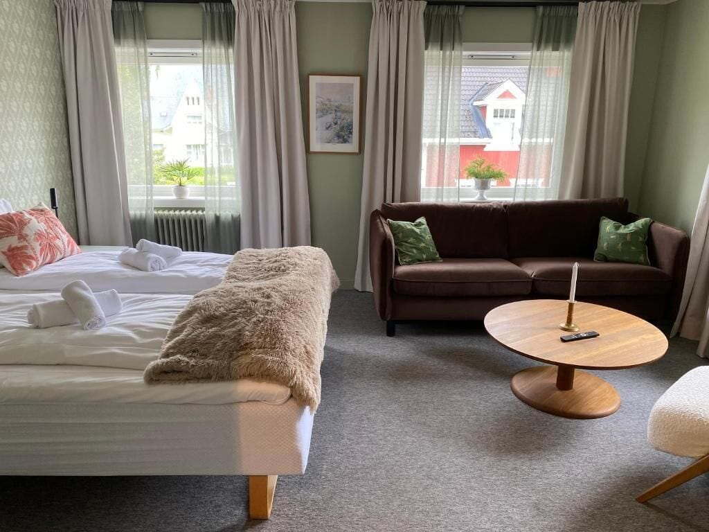 Quarto de hotel com uma cama, um sofá, uma mesa redonda de madeira e vista para o exterior.
