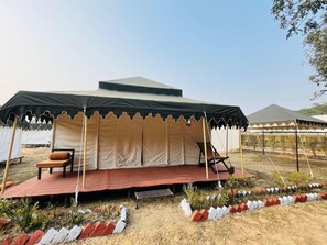 Uma tenda com plataforma e área de estar, rodeada por um jardim ajardinado.