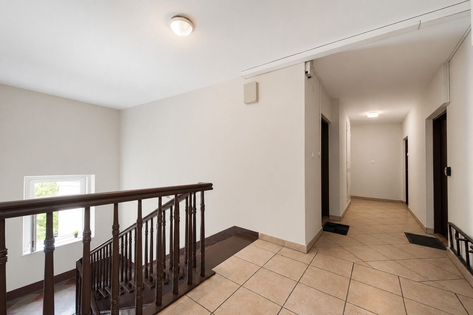 Um corredor com escada de madeira, luminária e uma porta no final.