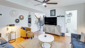 Uma sala de estar moderna com televisão, ventoinha no teto e escada que leva a um andar superior.