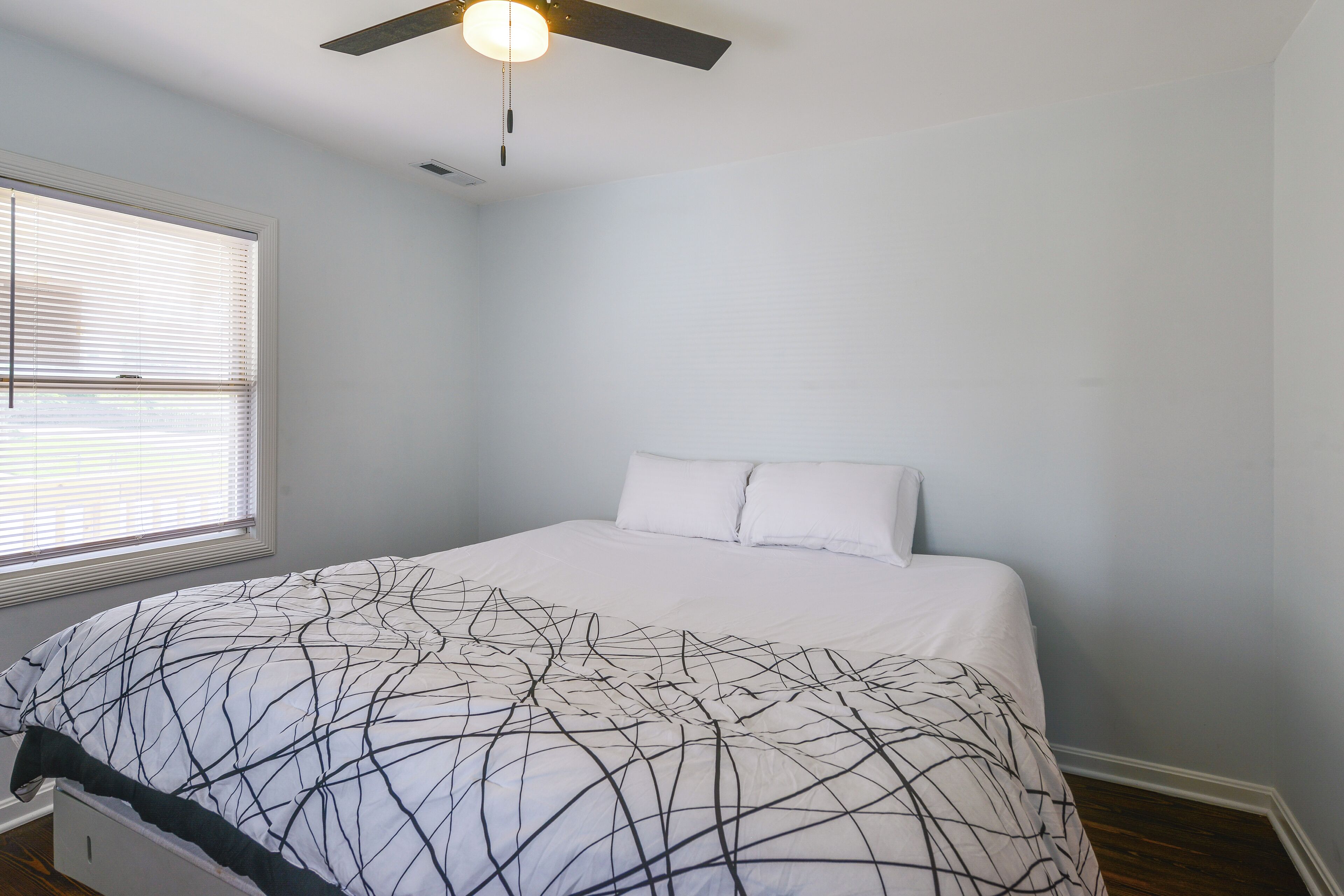Quarto com uma cama, ventilador de teto e janela com persianas.