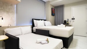 Quarto de hotel com duas camas, uma mesa de cabeceira, um abajur, um quadro e uma porta.