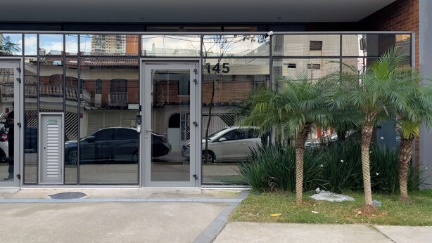 Entrada de um edifício com portas de vidro, o número '145' visível e carros estacionados.