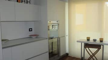 Uma cozinha com armários brancos, forno com porta de vidro e uma pequena mesa com xícaras.