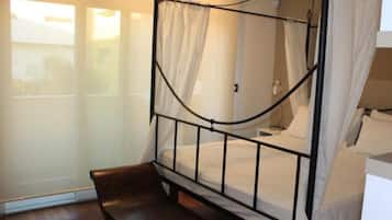 Quarto com cama de dossel, um banco e janela com cortinas.