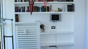 Um quarto com uma estante branca, uma televisão fixada na parede e uma janela com persianas.