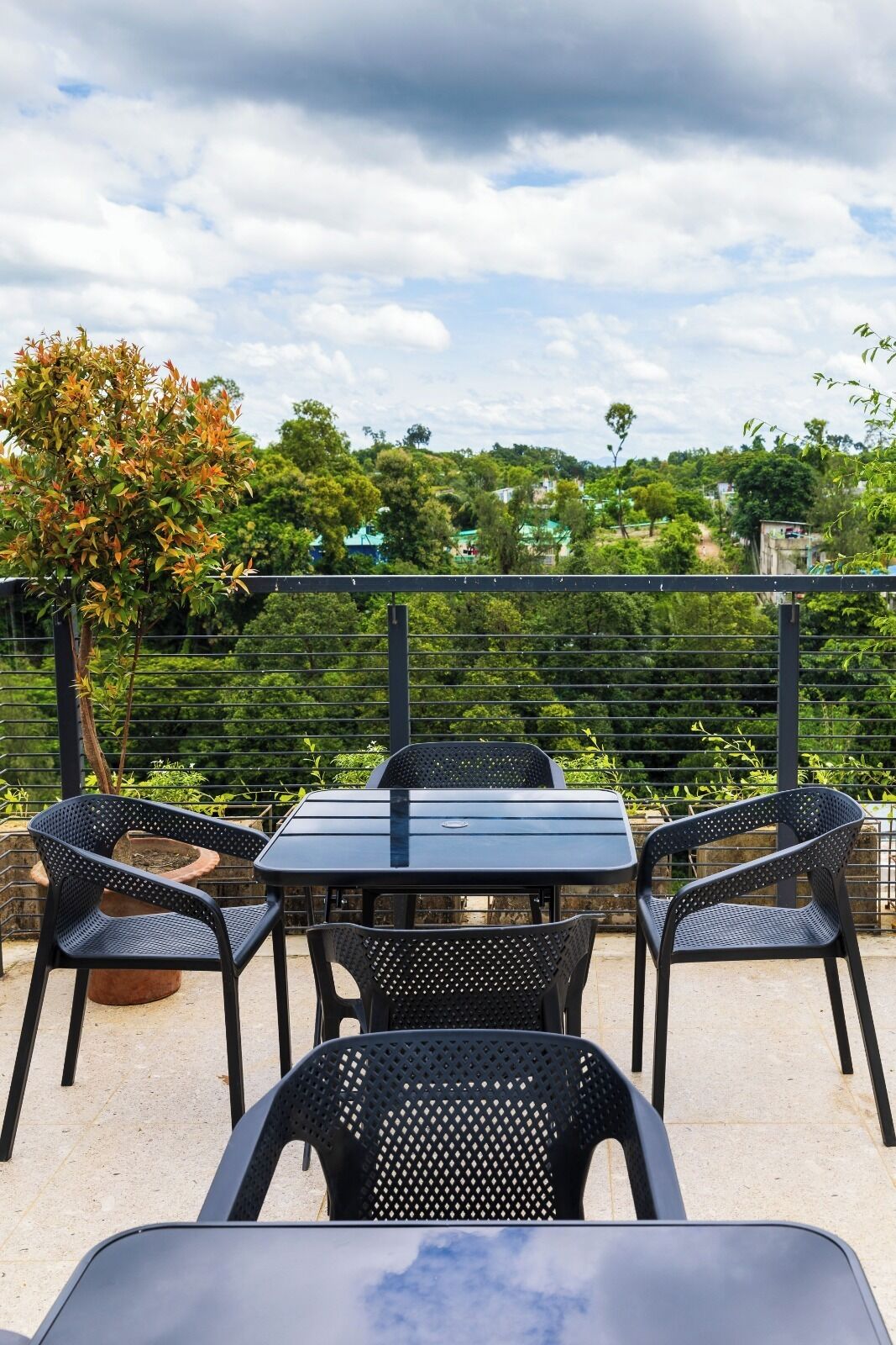 Um pátio externo com mesa e cadeiras, cercado por uma grade de metal e vegetação.
