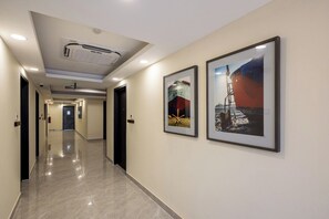 Corredor de hotel com piso encerado, obras de arte emolduradas nas paredes e unidade de ar condicionado no teto.