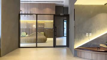 Interior moderno com uma mesa de recepção, área de estar com um sofá estampado e uma porta de vidro que dá para outro espaço.