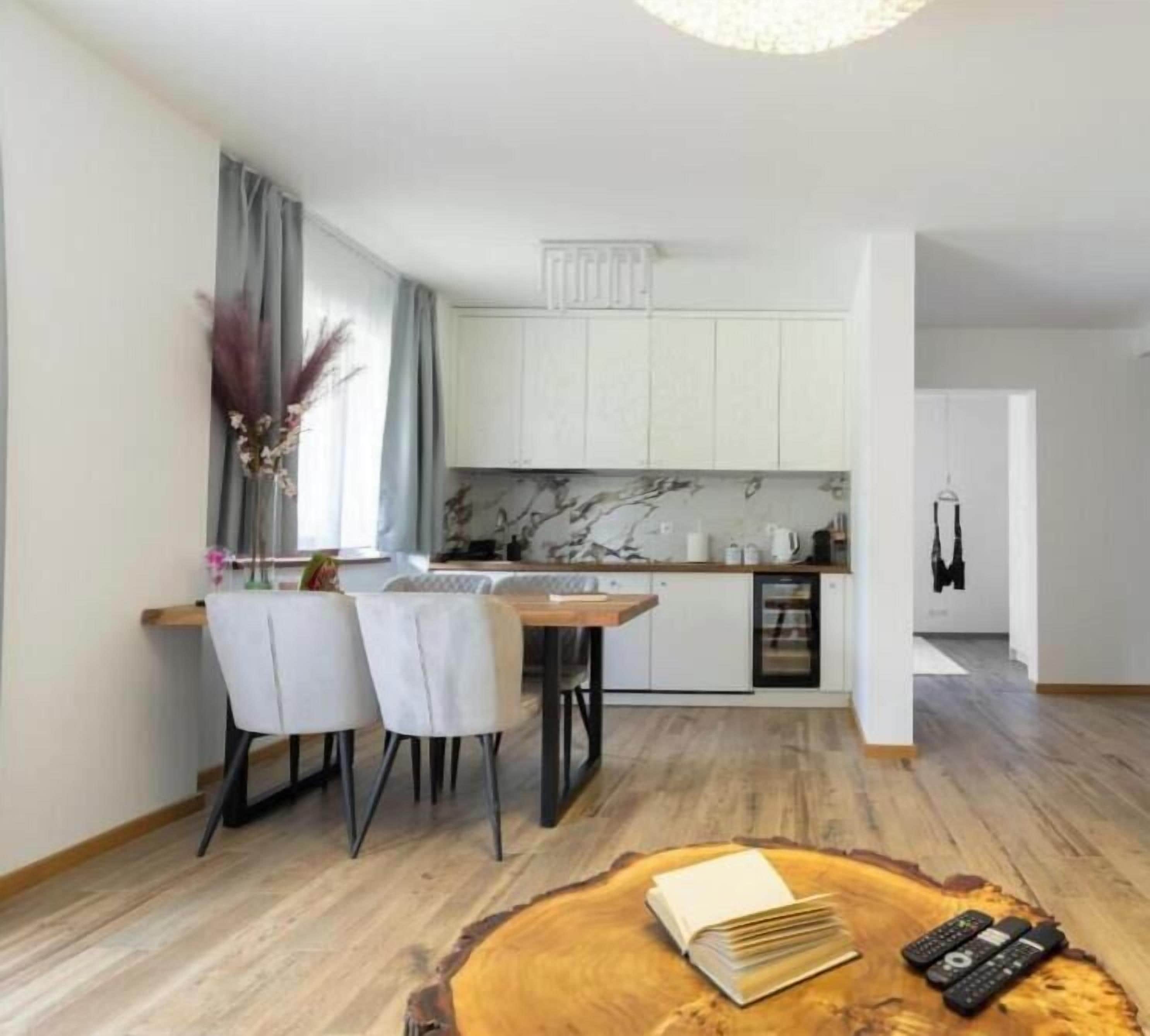 Uma cozinha moderna com armários brancos, painel de mármore e uma área de jantar com mesa e cadeiras de madeira.