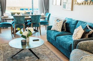 Uma sala de estar com um sofá azul-turquesa, poltronas a combinar, uma mesa de centro redonda e um espaço de jantar com mesa e cadeiras.